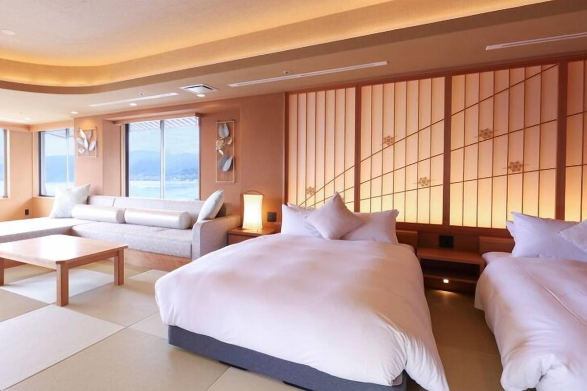 Quarto de hotel moderno com uma cama grande, um sofá, uma mesa de centro e vista para o exterior.