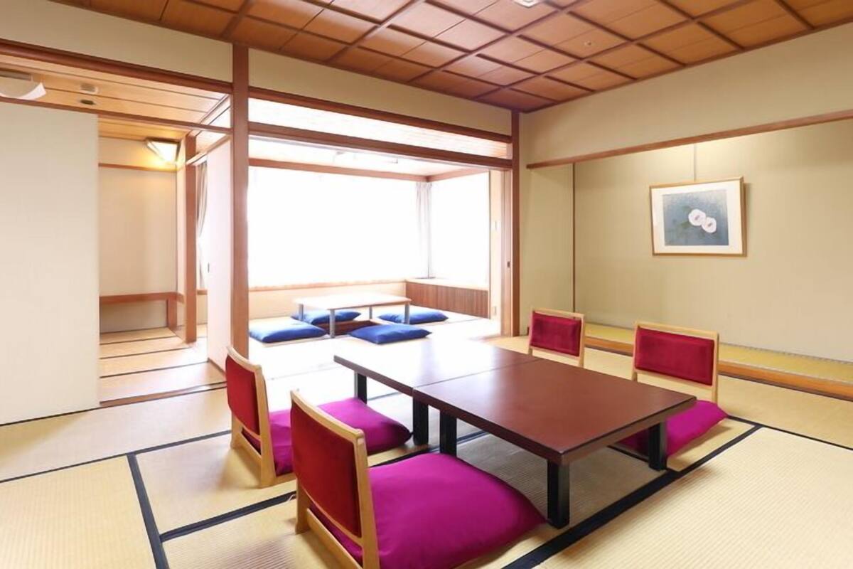 Um quarto japonês tradicional com soalho de tatame, uma mesa baixa e almofadas vermelhas.