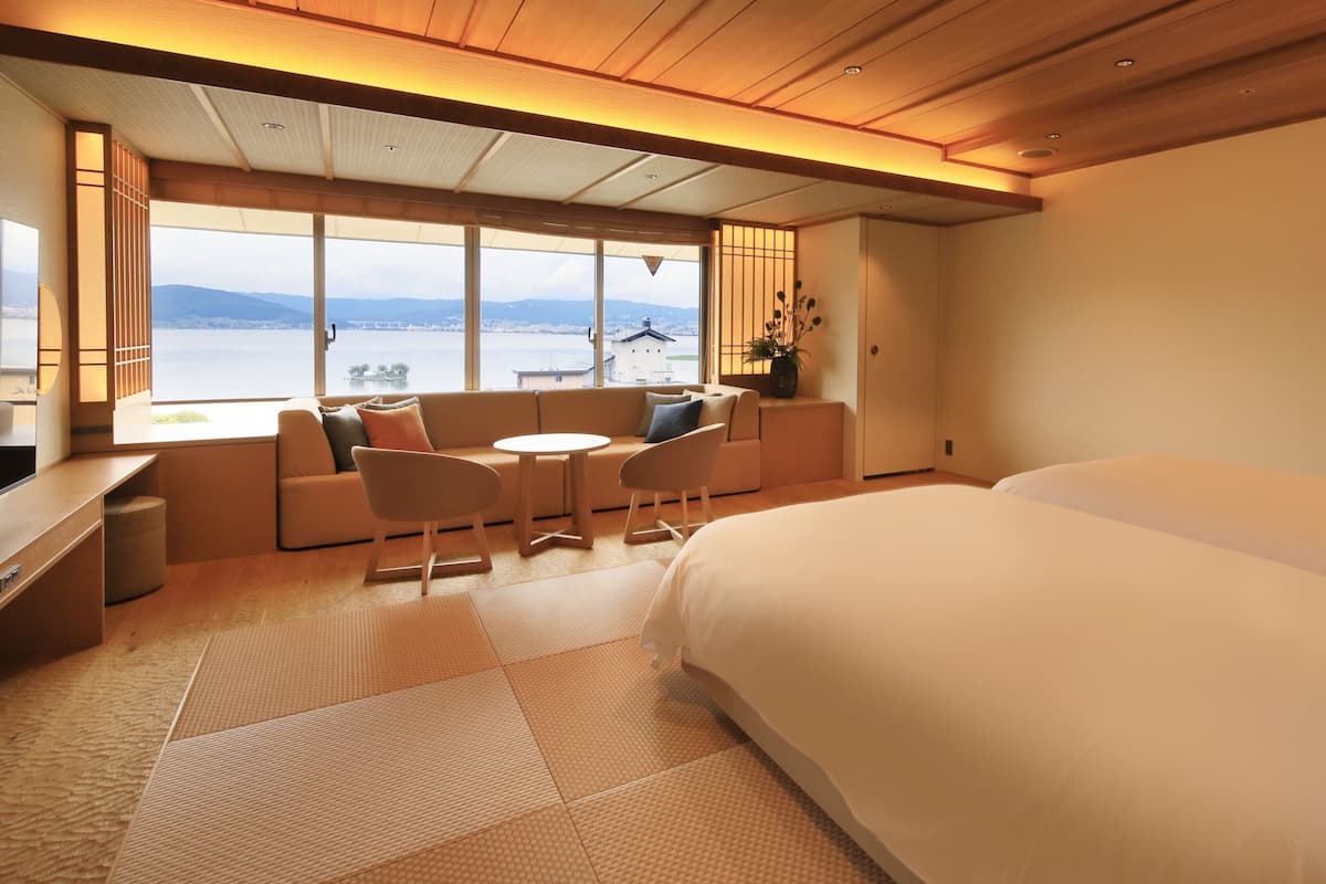 Quarto de hotel com uma cama grande, área de estar com uma mesa e vista para o mar.