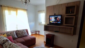Uma sala de estar com sofá, televisão fixada em uma parede de madeira e um pequeno armário de madeira.