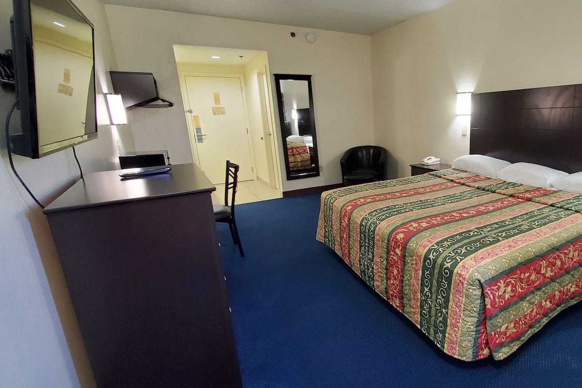 Quarto de hotel com uma cama grande, uma escrivaninha com cadeira, espelho, guarda-roupa e mesa de cabeceira.