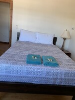 Cama bem arrumada com roupa de cama estampada, duas toalhas dobradas e uma luminária de cabeceira.