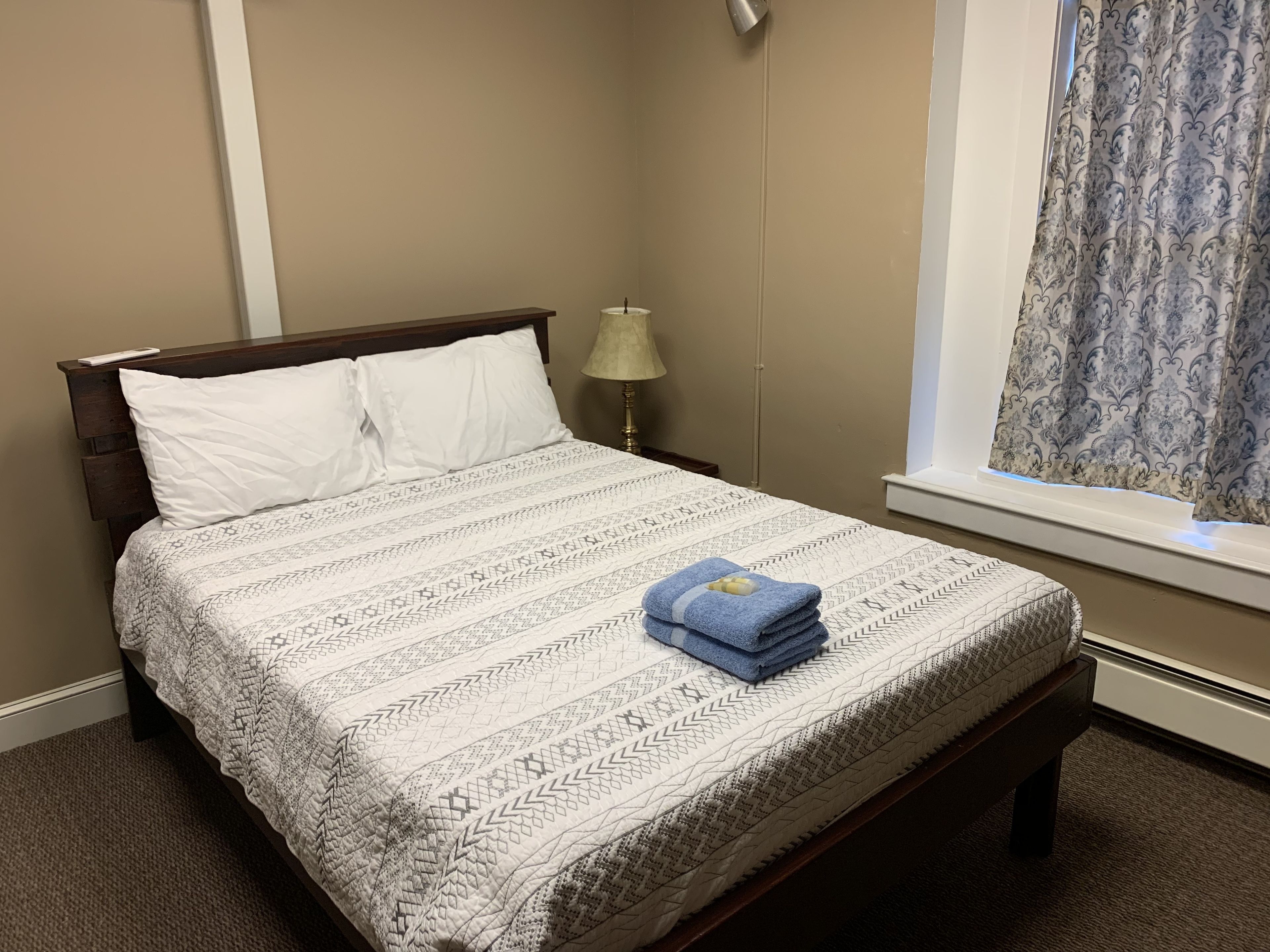 Cama bem arrumada com colcha estampada, duas almofadas e uma toalha dobrada na peseira.