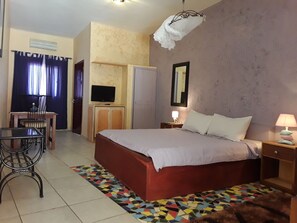 Quarto de hotel com cama, escrivaninha, cadeira, televisão, guarda-roupa e espelho.