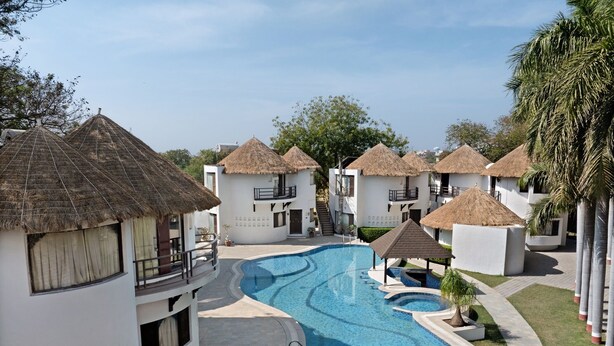Um resort com piscina, bangalôs de telhado de palha e céu claro.