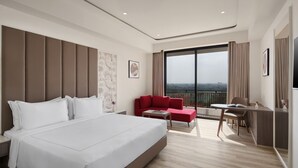 Quarto de hotel moderno com uma cama grande, um sofá vermelho, uma escrivaninha e uma varanda com vista.