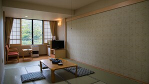 Um quarto japonês tradicional com tatames, uma mesa baixa com televisão, um sofá e uma porta deslizante.