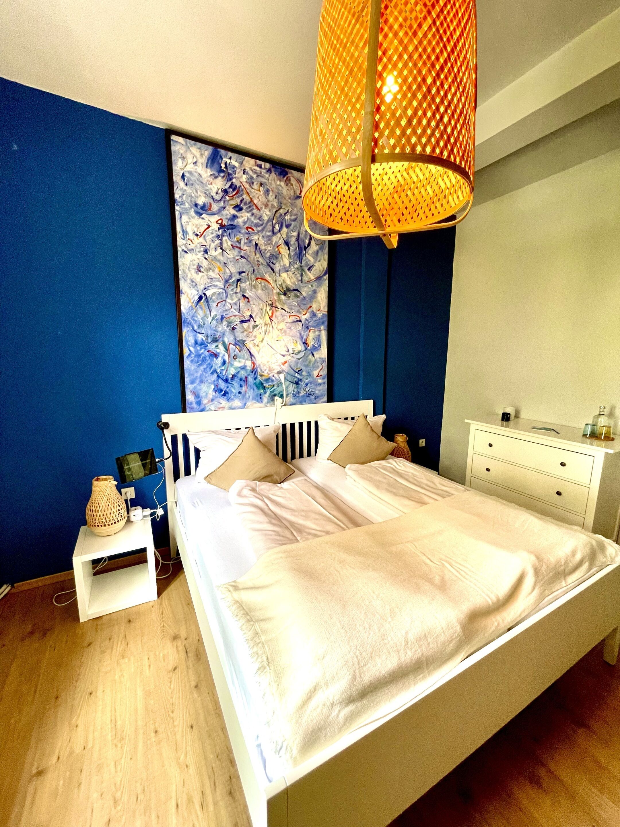 Um quarto com uma cama, mesas de cabeceira, uma luminária e um quadro na parede.