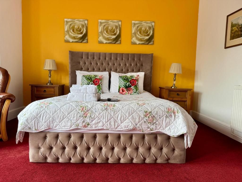 Quarto com cabeceira estofada, colcha florida e três quadros de rosas pendurados na parede.