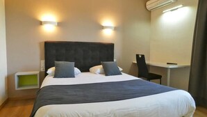Quarto de hotel com uma cama grande, duas luminárias de cabeceira, uma escrivaninha e um ar condicionado.