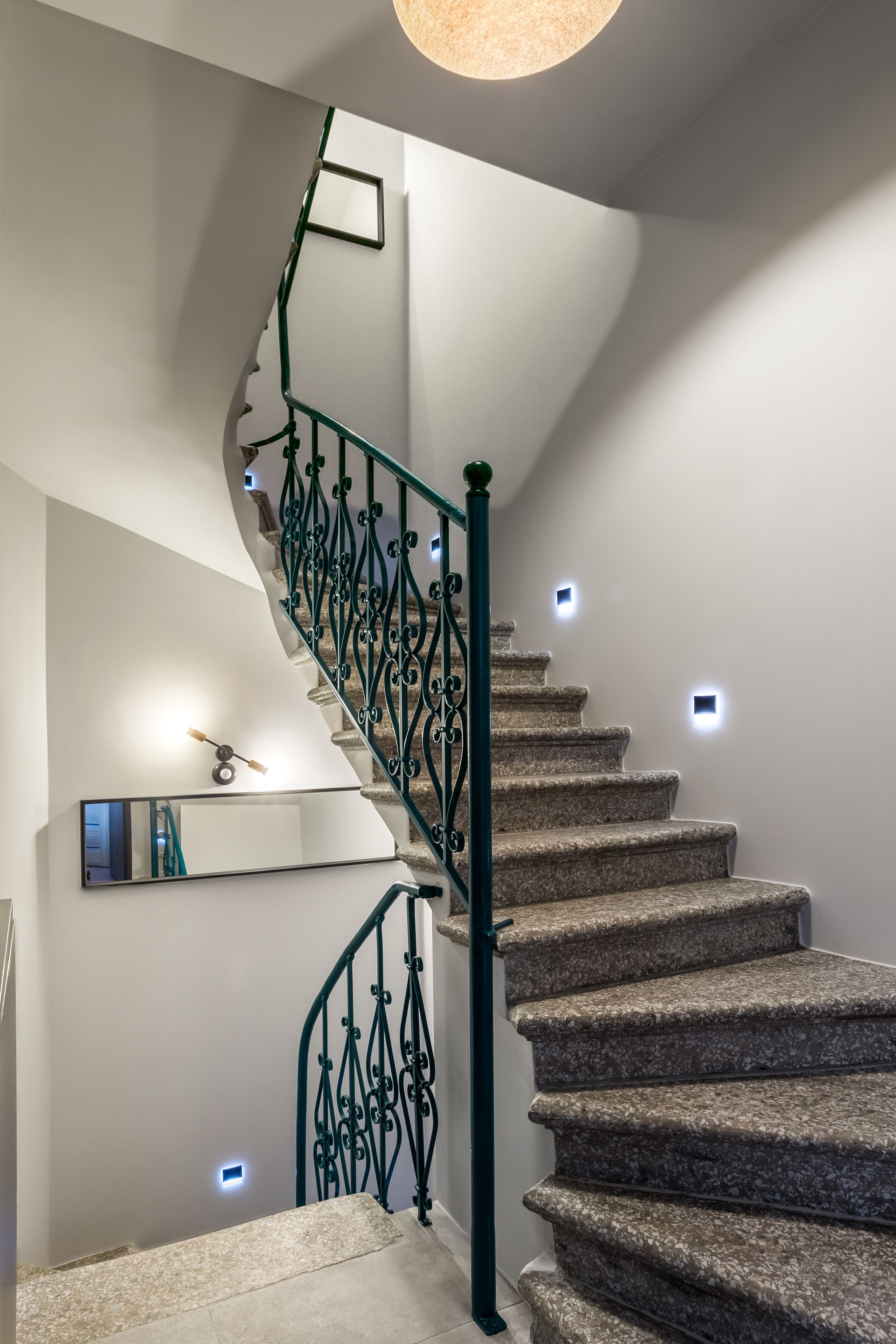 Uma escadaria em espiral com guarda-corpo de metal verde e iluminação embutida.