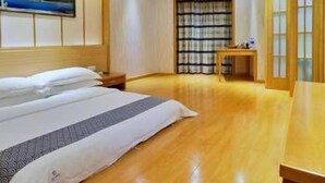 Quarto de hotel com uma cama grande, piso de madeira, um quadro na parede, uma janela com cortinas e uma porta de madeira.