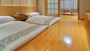 Quarto de hotel com duas camas, soalho de madeira, um quadro na parede e vista através de uma porta.