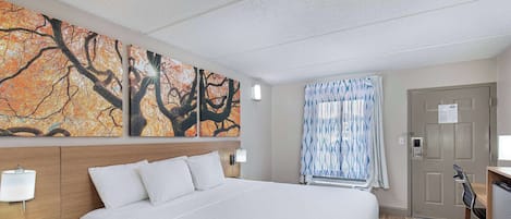 Quarto de hotel com uma cama grande, mesa de cabeceira, escrivaninha e televisão fixada na parede.