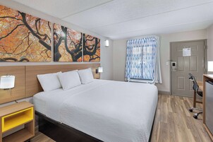 Quarto de hotel com uma cama grande, mesa de cabeceira, escrivaninha e televisão fixada na parede.