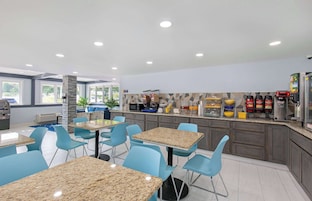 Cozinha moderna com bancadas de granito, cadeiras azuis e diversos eletrodomésticos, incluindo micro-ondas, cafeteira e geladeira.