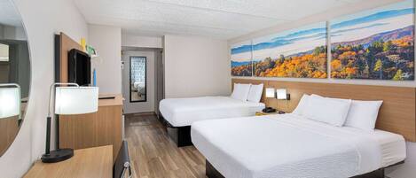 Quarto de hotel com duas camas, uma escrivaninha com abajur, um espelho e um quadro com folhagem de outono na parede.