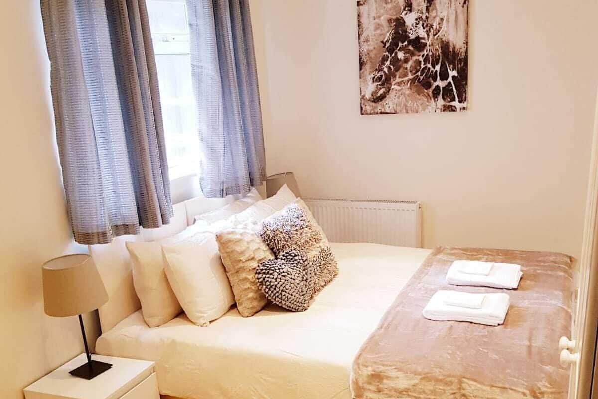 Quarto com cama, mesa de cabeceira, luminária e tapete estampado com flores.