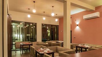 Um restaurante com várias mesas, cadeiras e luminárias pendentes.