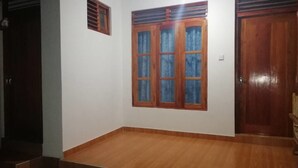 Um quarto com piso de madeira, janela emoldurada por madeira e uma porta.