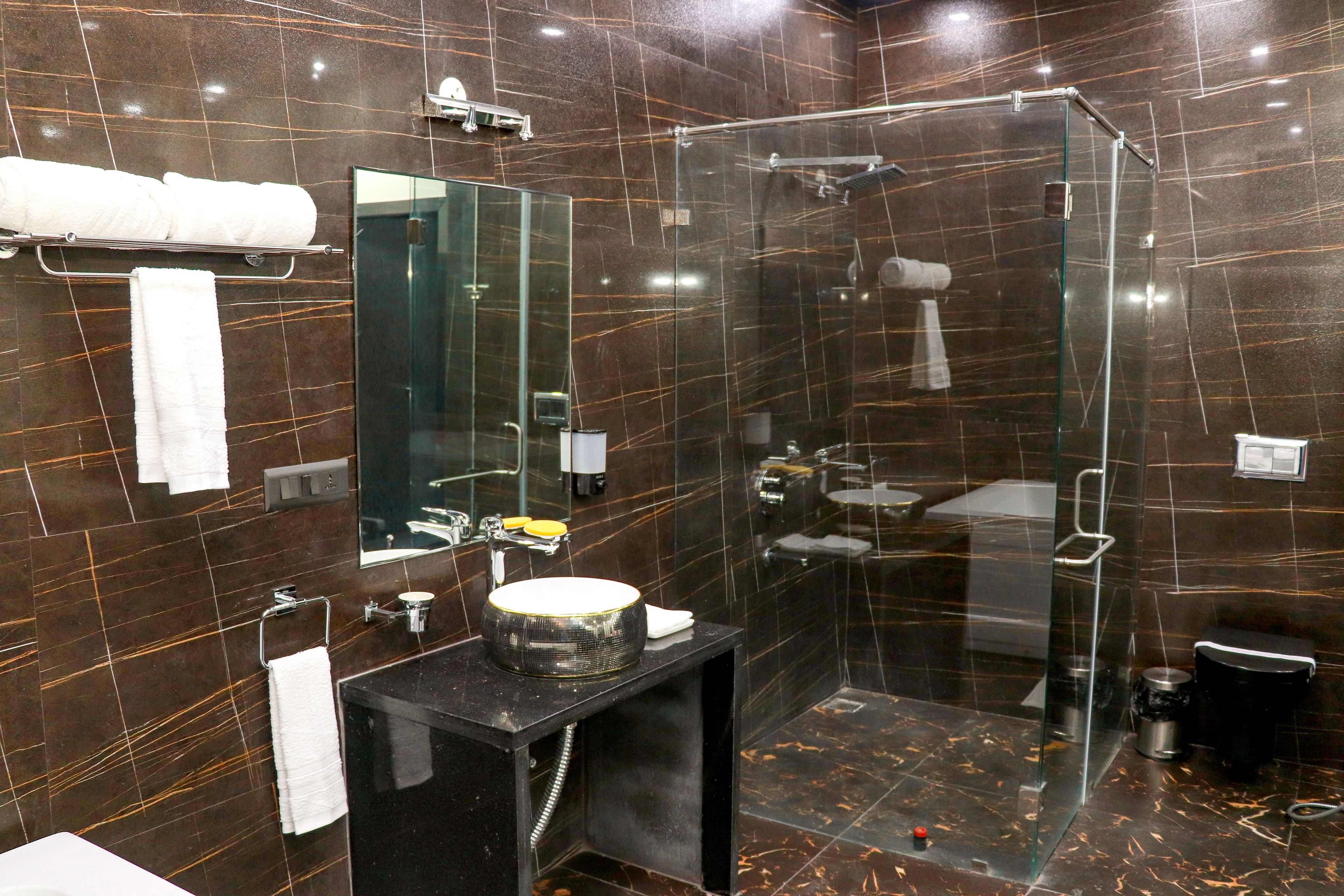 Uma casa de banho moderna com chuveiro em cabine de vidro, um espelho grande e toucador preto com lavatório.