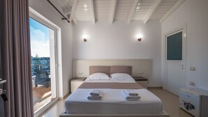 Quarto de hotel com uma cama grande, duas mesas de cabeceira, um guarda-roupa e uma porta de vidro deslizante para o exterior.