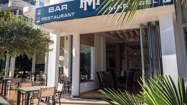 Um bar e restaurante com mesas ao ar livre, uma palmeira e um céu azul límpido.