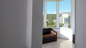 Quarto de hotel com um espelho grande, uma mesa de vidro com garrafas e vista da cidade por grandes janelas.
