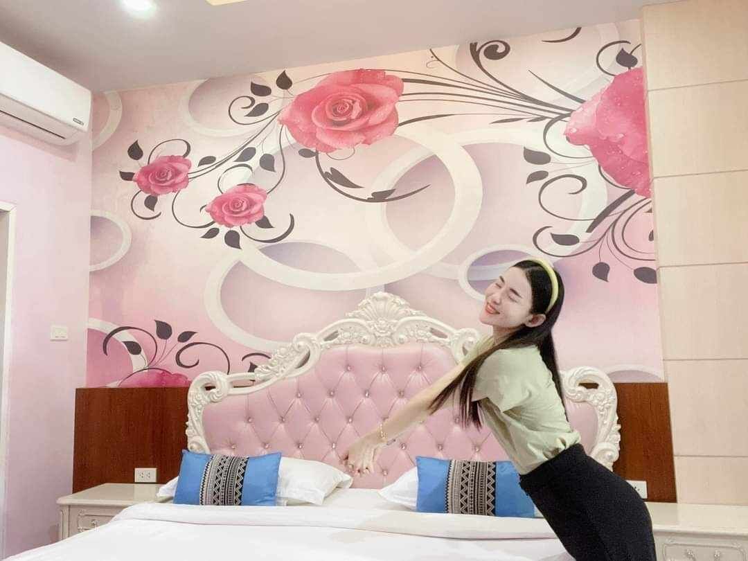 Quarto com design floral rosa e branco nas paredes, cabeceira estofada e cama com roupa de cama azul e branca.