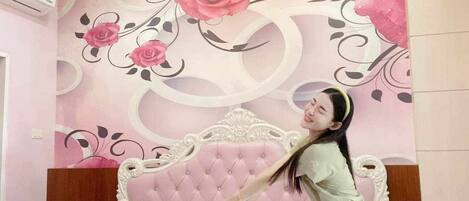 Quarto com design floral rosa e branco nas paredes, cabeceira estofada e cama com roupa de cama azul e branca.