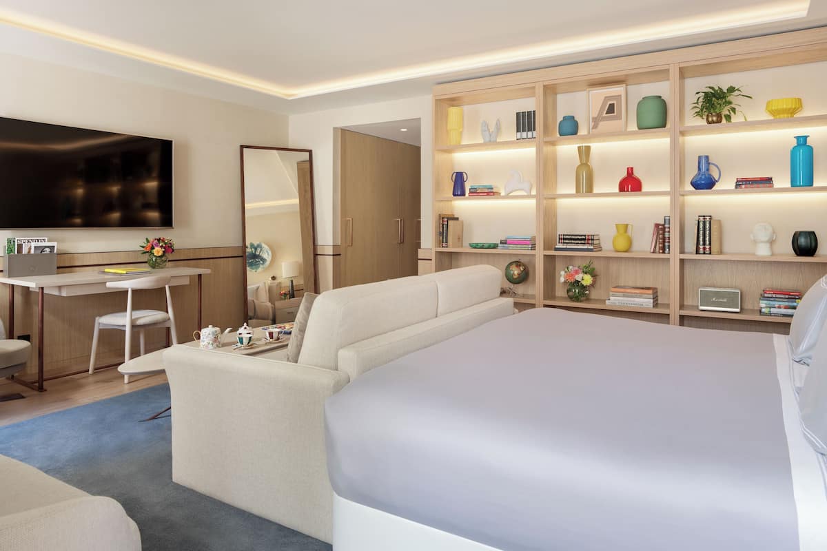 Quarto de hotel moderno com uma cama grande, uma escrivaninha, uma cadeira e uma estante de livros.
