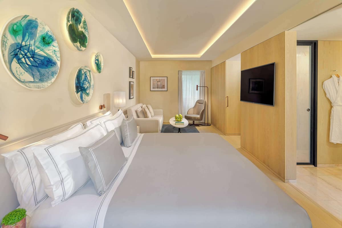 Quarto de hotel moderno com uma cama grande, um sofá, uma televisão e obras de arte nas paredes.