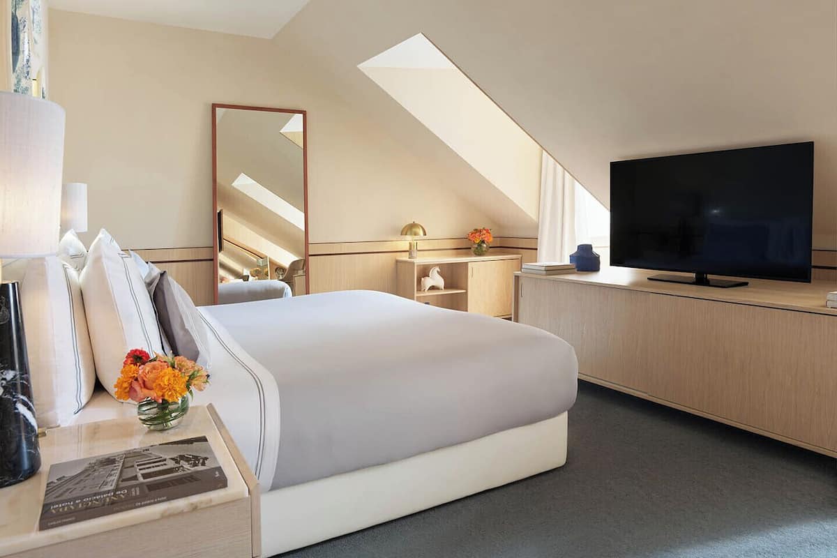 Quarto de hotel moderno com uma cama grande, uma TV de tela plana, uma escrivaninha com abajur e um espelho.