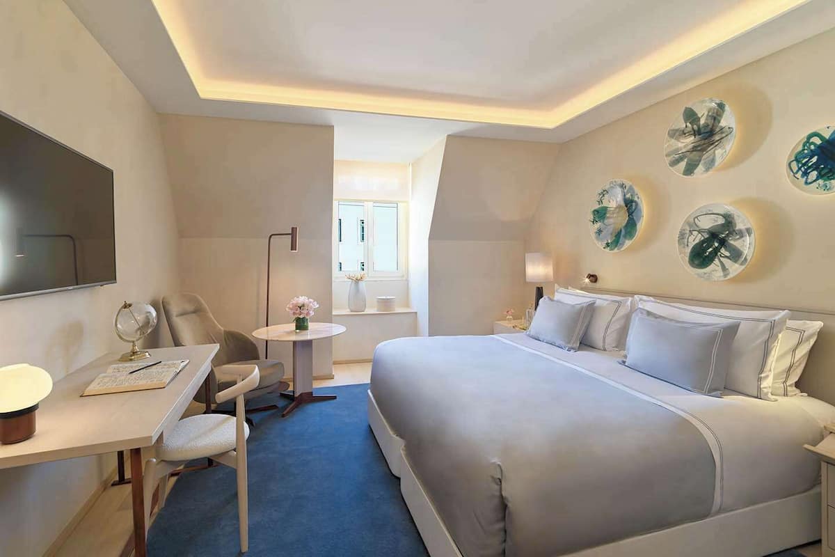 Quarto de hotel moderno com uma cama grande, uma escrivaninha e uma cadeira. Há uma janela com vista para o exterior.