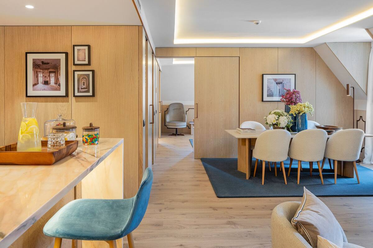 Quarto de hotel moderno com piso de madeira, área de refeições com mesa e cadeiras e cozinha compacta com bancada.