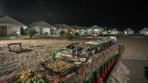 Buffet montado em uma praia arenosa, com tendas ao fundo.