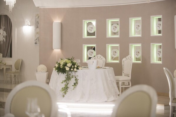 Decoração de recepção de casamento com mesa florida, cadeiras ao redor e arte floral na parede.