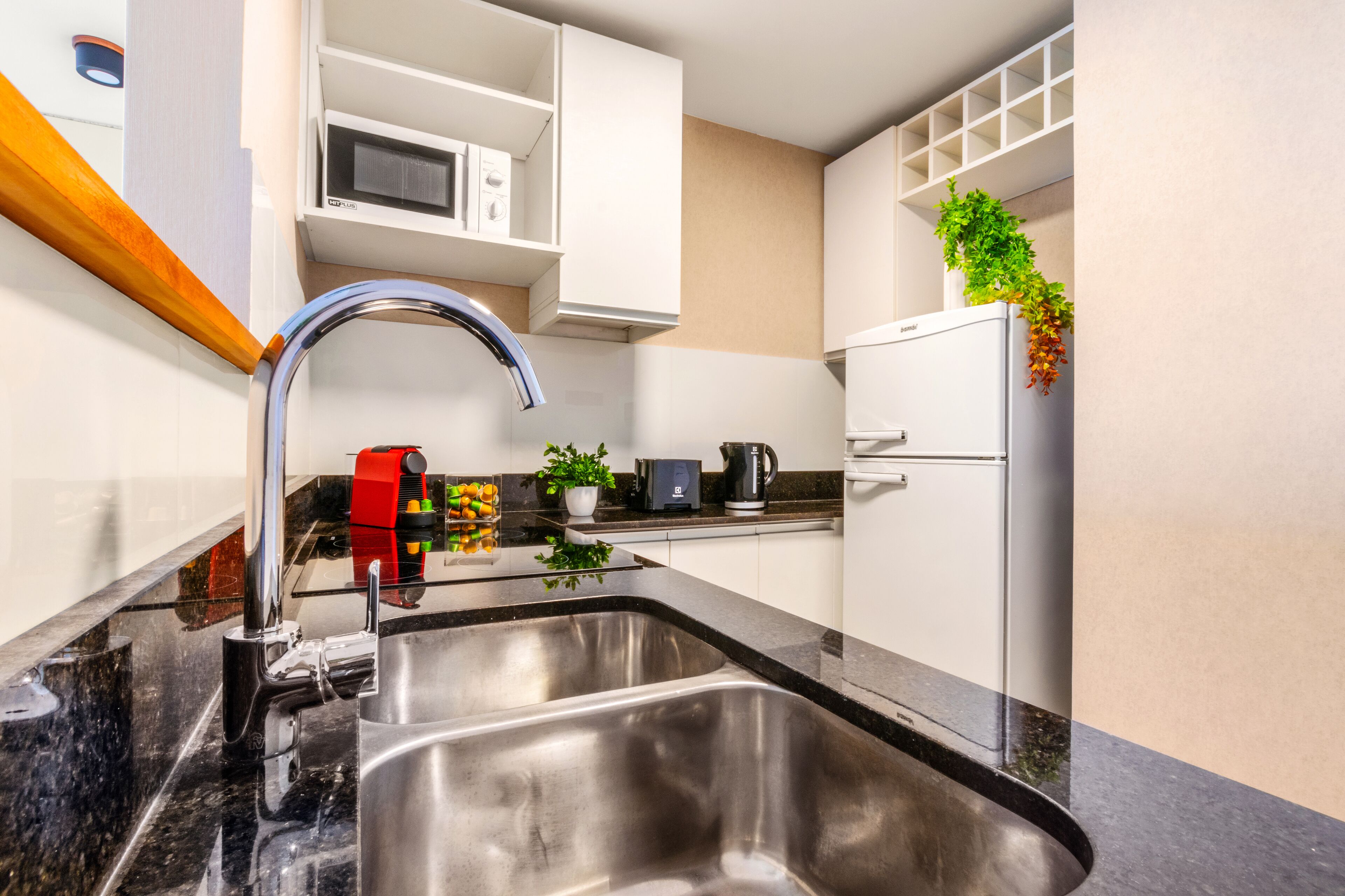 Uma cozinha moderna com pias de aço inoxidável, micro-ondas e geladeira.