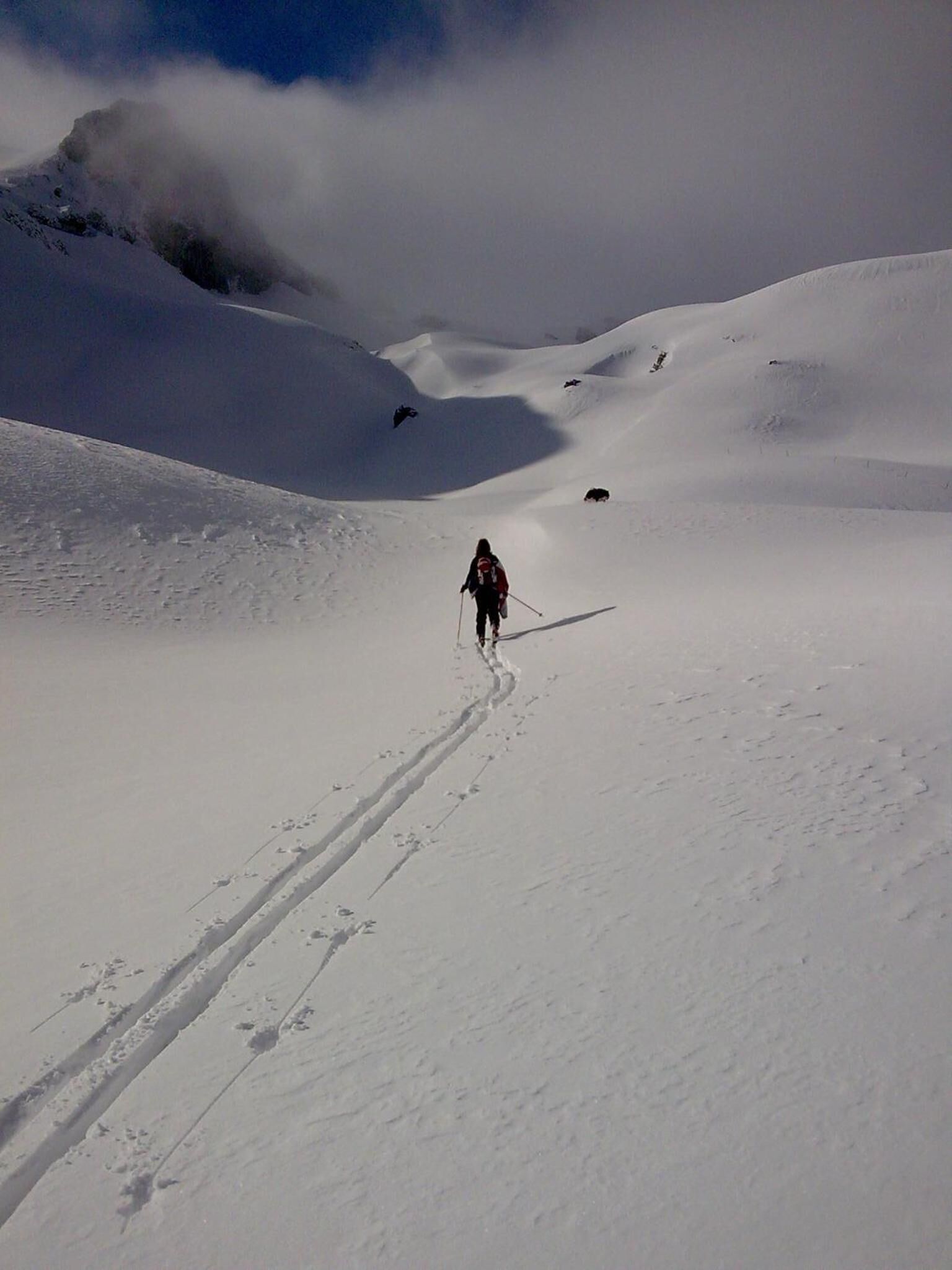 Uma trilha nevada na montanha com um único esquiador.