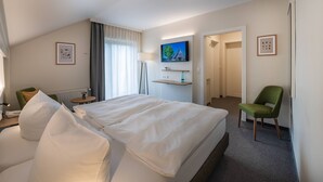 Quarto de hotel com cama, televisão, cadeira, escrivaninha e porta que dá para outro quarto.