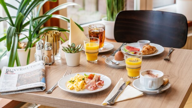 Uma mesa de café da manhã com pratos de comida, copos de suco de laranja, um jornal e uma xícara de café.
