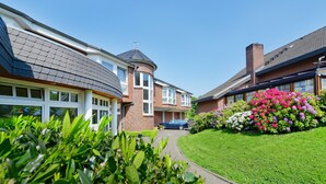 Um bairro residencial com casas, entrada de automóveis e um gramado bem cuidado com flores coloridas.