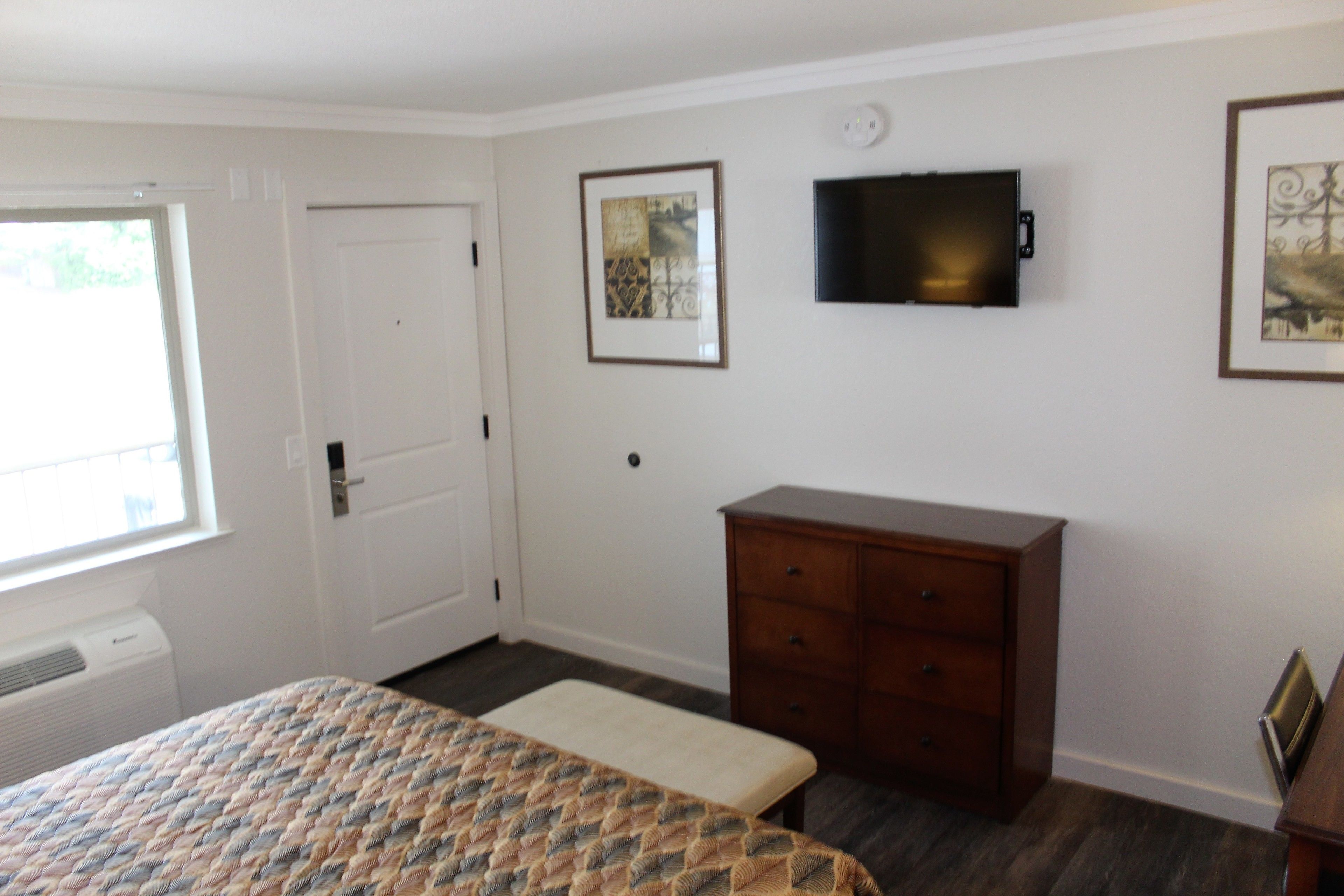 Quarto com cama, penteadeira, televisão e obras de arte nas paredes.