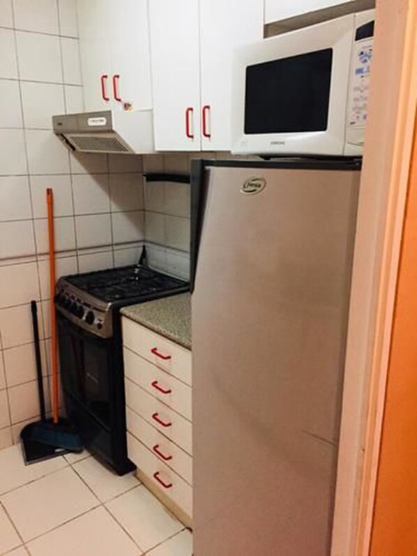 Uma cozinha compacta com fogão, micro-ondas e frigorífico.