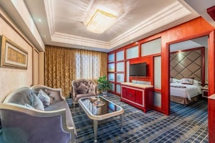 Quarto de hotel com sofá, poltrona, televisão e uma cama com um armário vermelho.