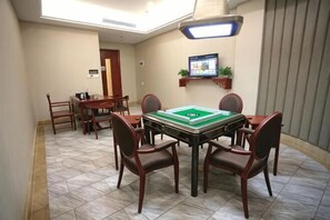 Quarto com mesa de bilhar, quatro cadeiras, televisão e uma pequena planta.