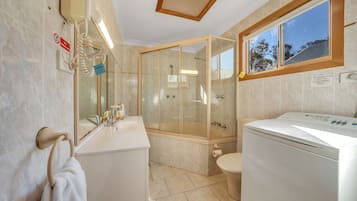 Casa de banho com chuveiro em cabine de vidro, sanita e máquina de lavar roupa.
