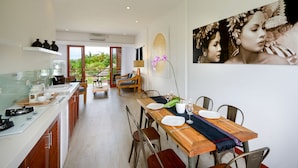 Cozinha moderna com área de refeições, mesa de madeira, cadeiras e vista para o verde lá fora.
