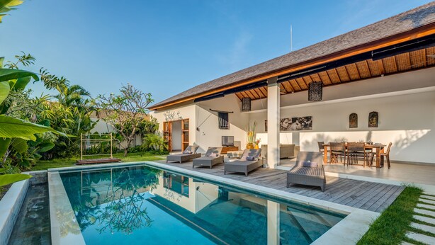 Uma área de piscina moderna ao ar livre, com espreguiçadeiras e um deck de madeira, rodeada por vegetação exuberante.