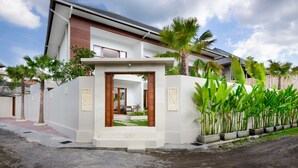 Uma casa moderna com fachada branca, porta de madeira e um pequeno jardim com palmeiras.